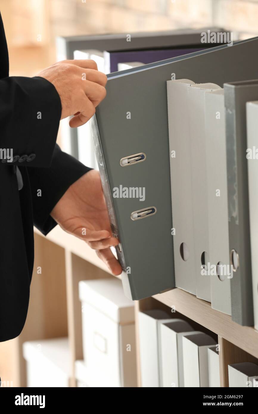 Young man taking folder with documents from shelf in archive Stock ...