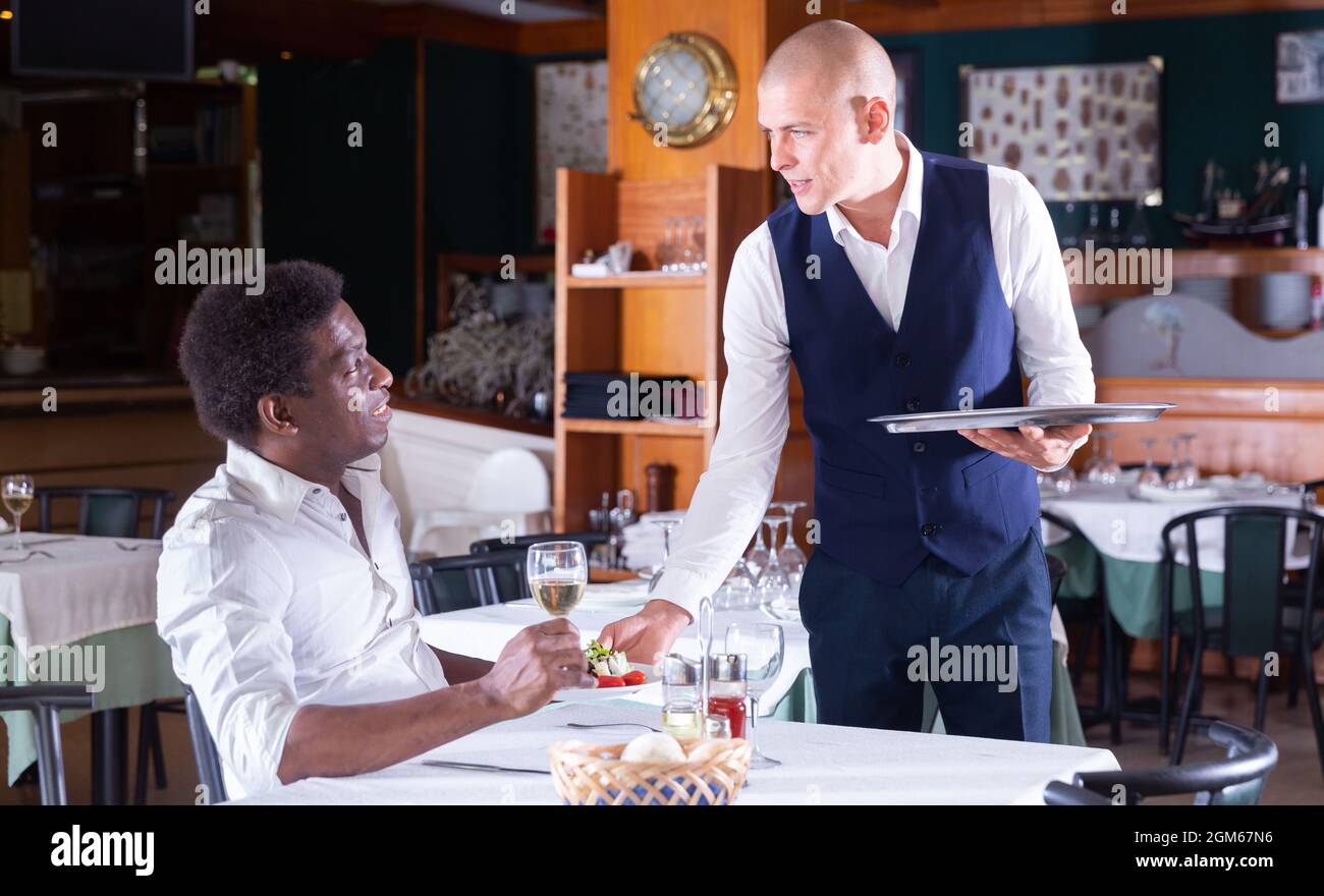 Friendly waiter serving cheerful African American in restaurant Stock ...
