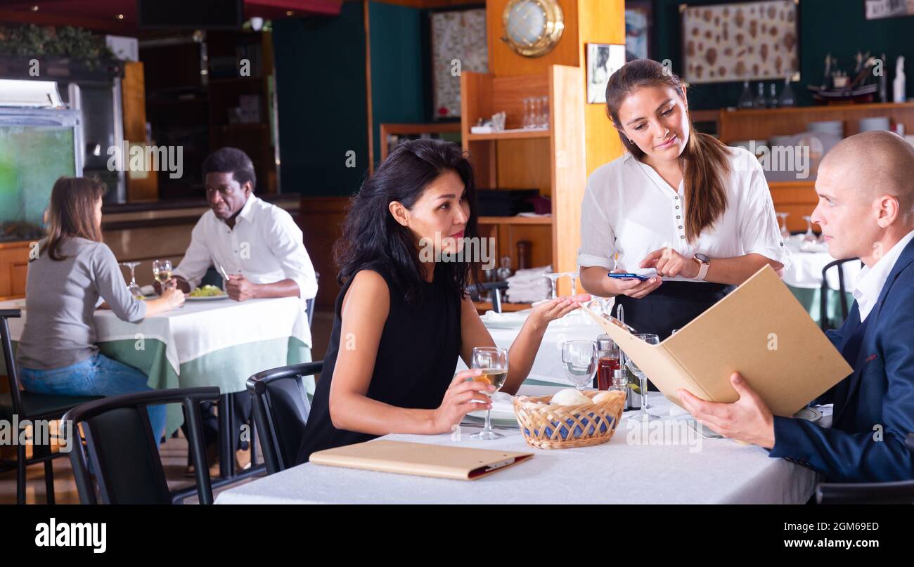 positive female busboy taking order to couple in modern restaurante ...