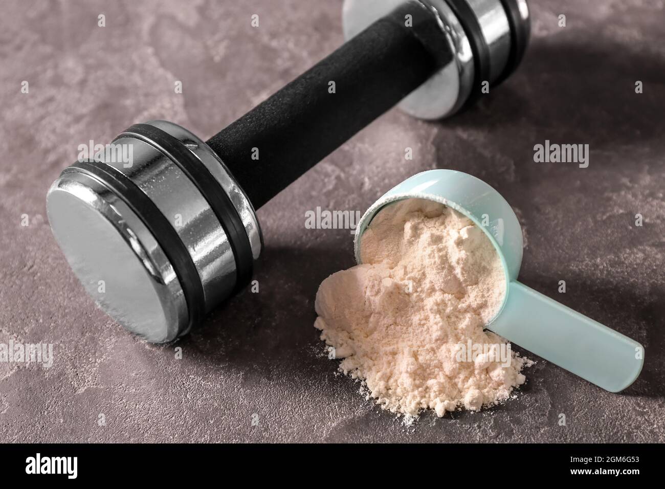 Measuring scoop with protein powder and dumbbell on grey background ...