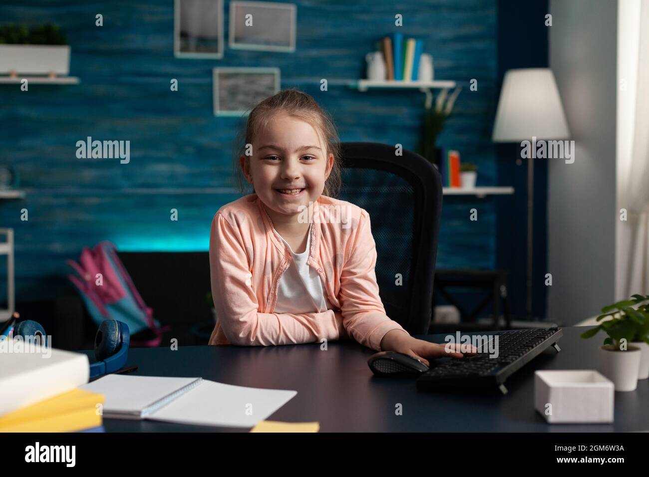 Portrait of smiling little schoolchild sitting at desk table in living ...