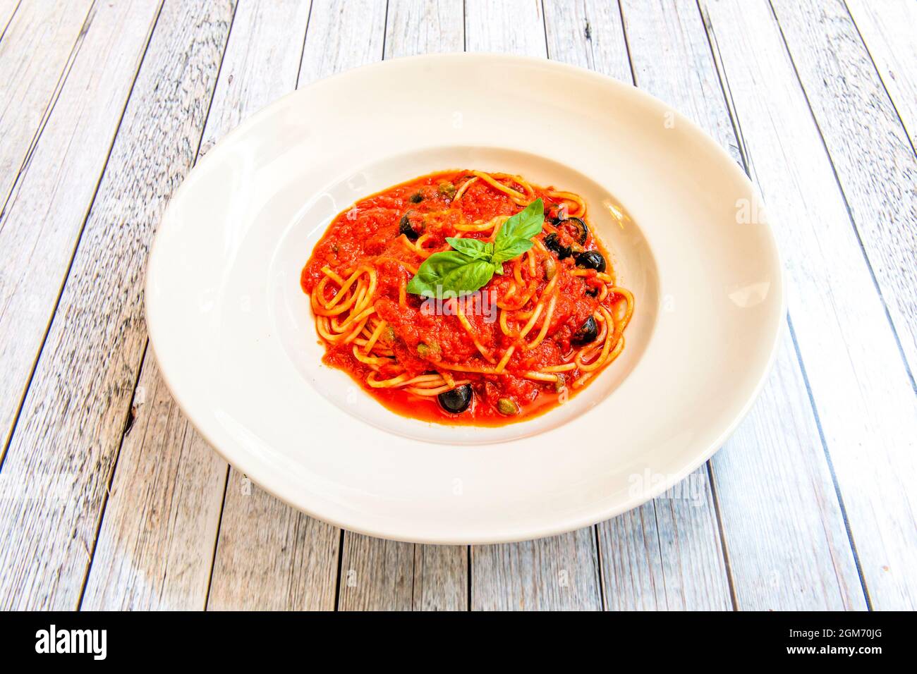White plate with tomato puttanesca spaghetti and black olives with ...