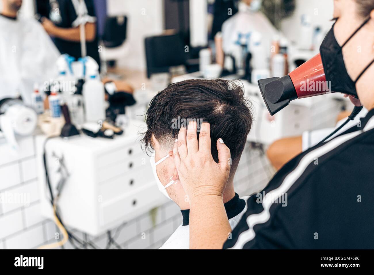 Hairdresser with mask drying the hair of a male with mask sitting in a ...