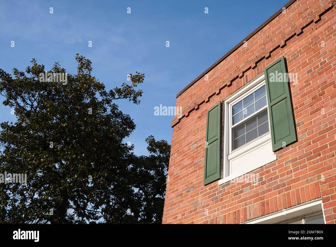 A corner window with wood green shutters of an old red brick garden ...