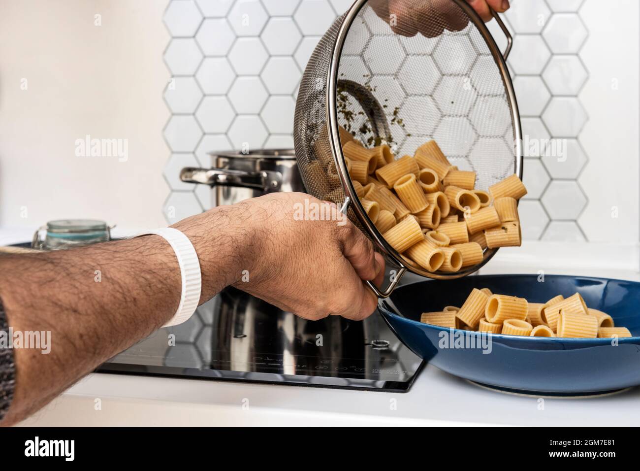 Man's hands pouring cooked pasta with oregano into a blue plate on top ...