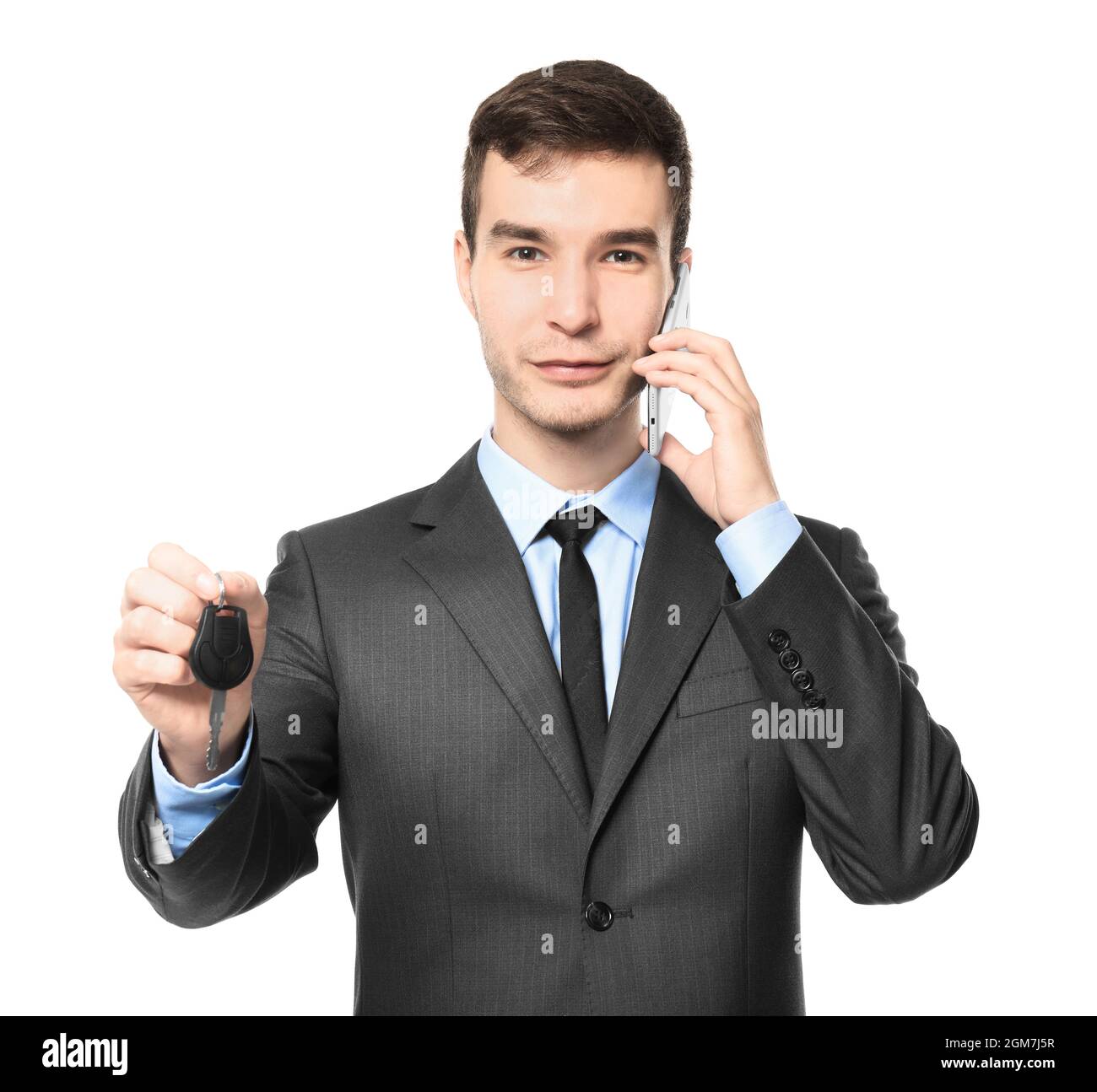 Handsome car salesman with key talking on mobile phone against white ...