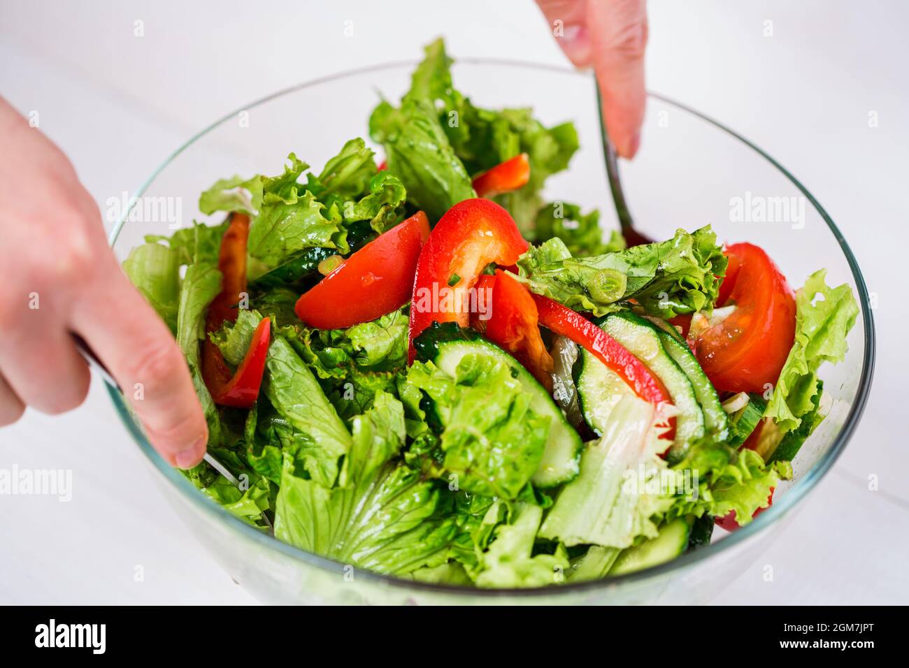 Young woman dressing vegetable salad with olive oil on a white ...