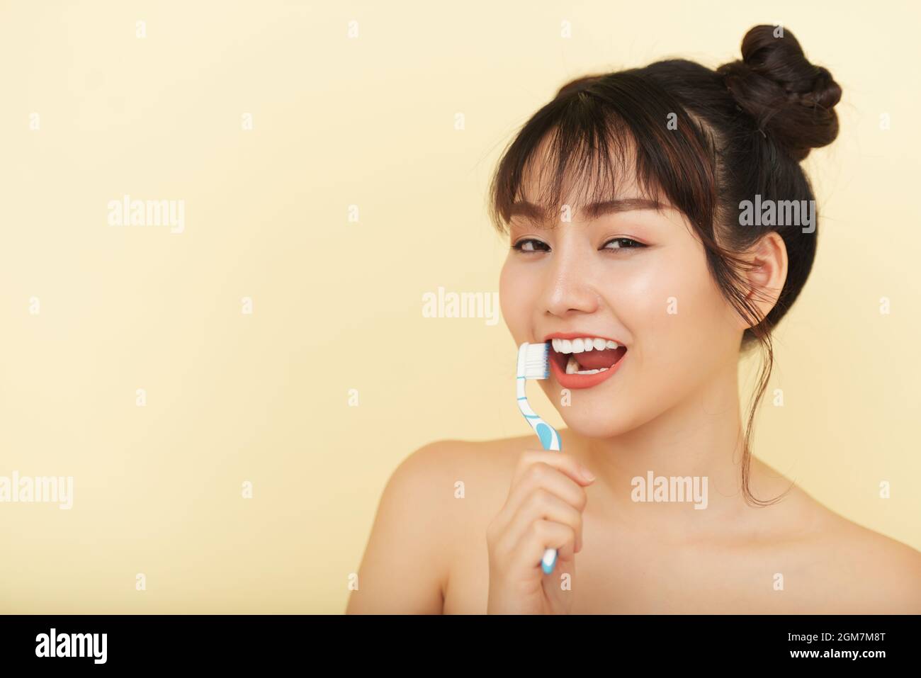 Pretty positive young Asian woman brushing teeth with whitening ...
