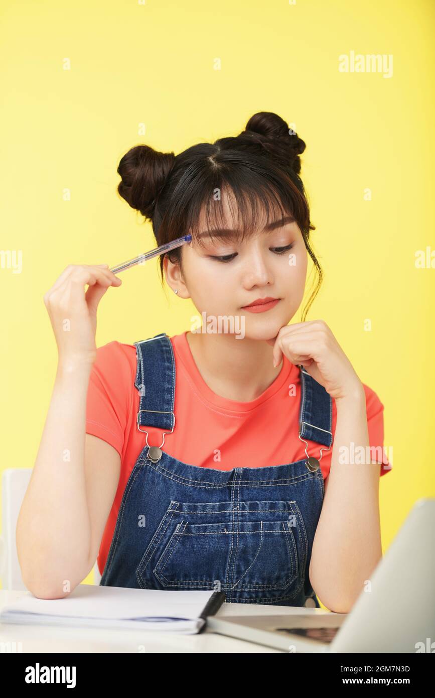 Portrait of pensive young Asian teenage girl doing homework and ...