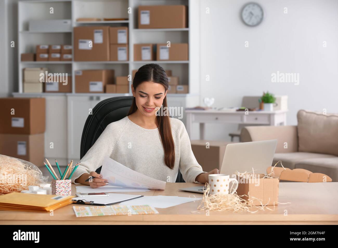Young woman with laptop preparing parcels for shipment to client in ...