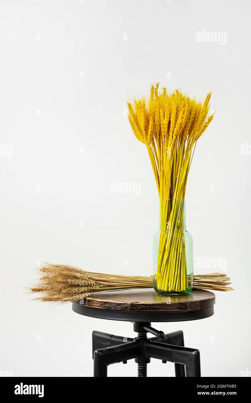 wheat bouquets inside a green vase and on a black industrial stool with ...