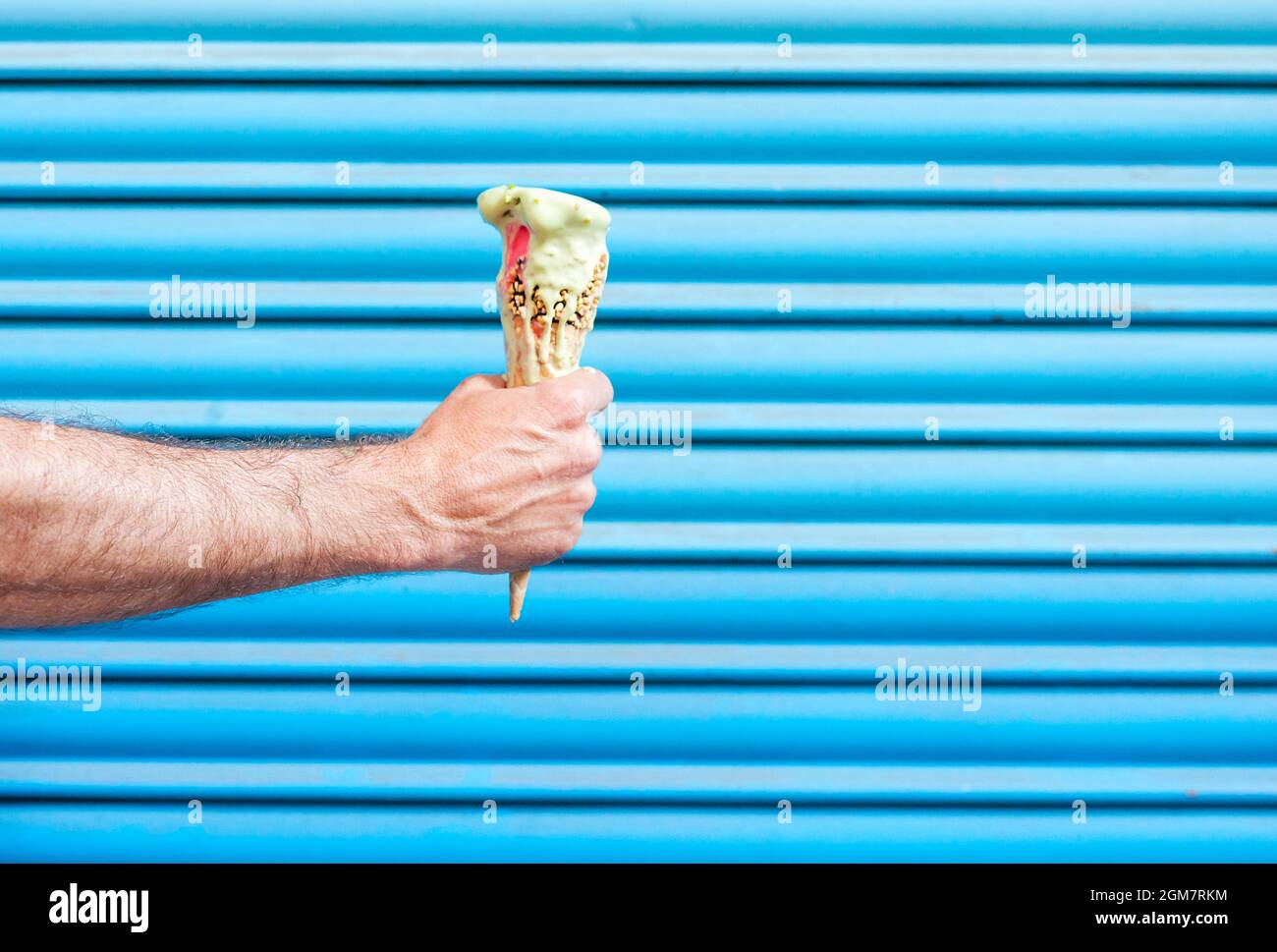 Mans Hand Holding An Ice Cream Cone Melting Over A Light Blue