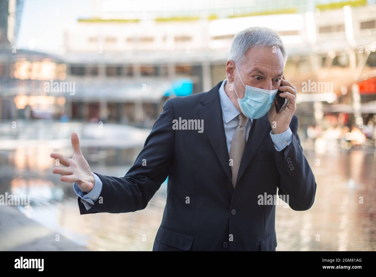 Angry masked senior business man yelling at the phone outdoor, covid ...
