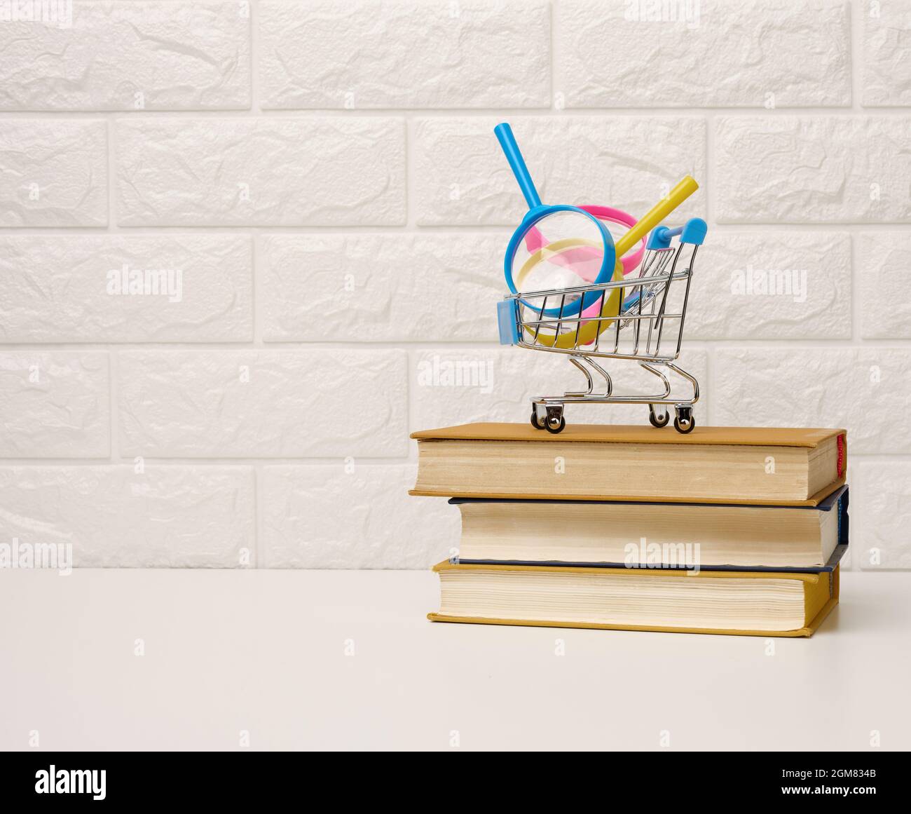 miniature shopping cart stands on a stack of books, white brick ...