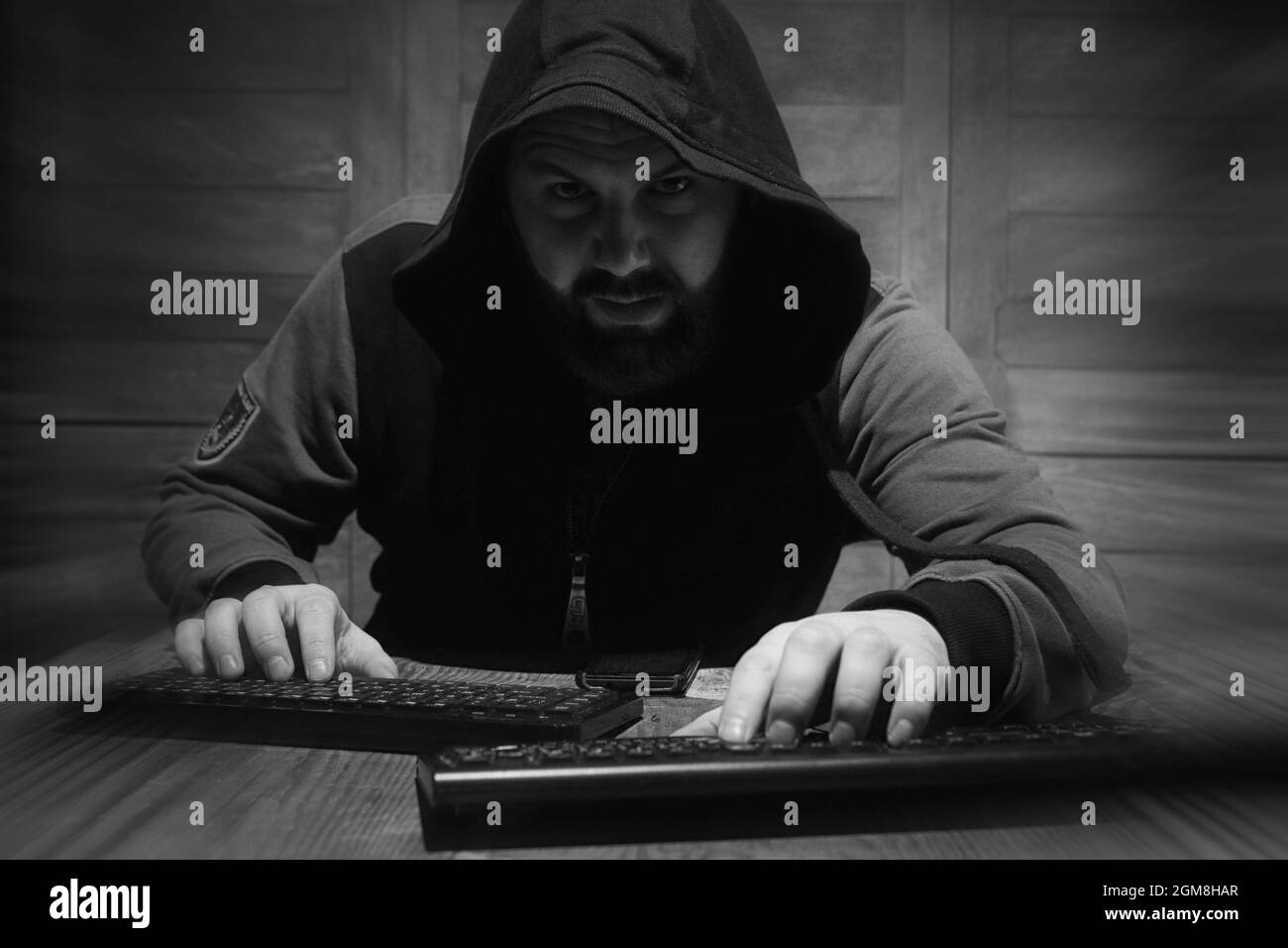 The hacker in the hood sits and works behind the computer Stock Photo ...