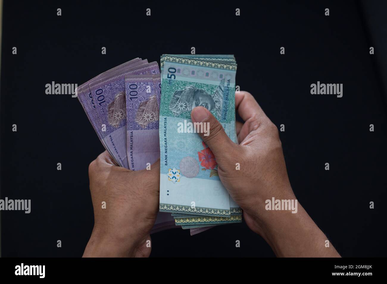 Closeup of man's hands counting Malaysian banknotes on a black ...