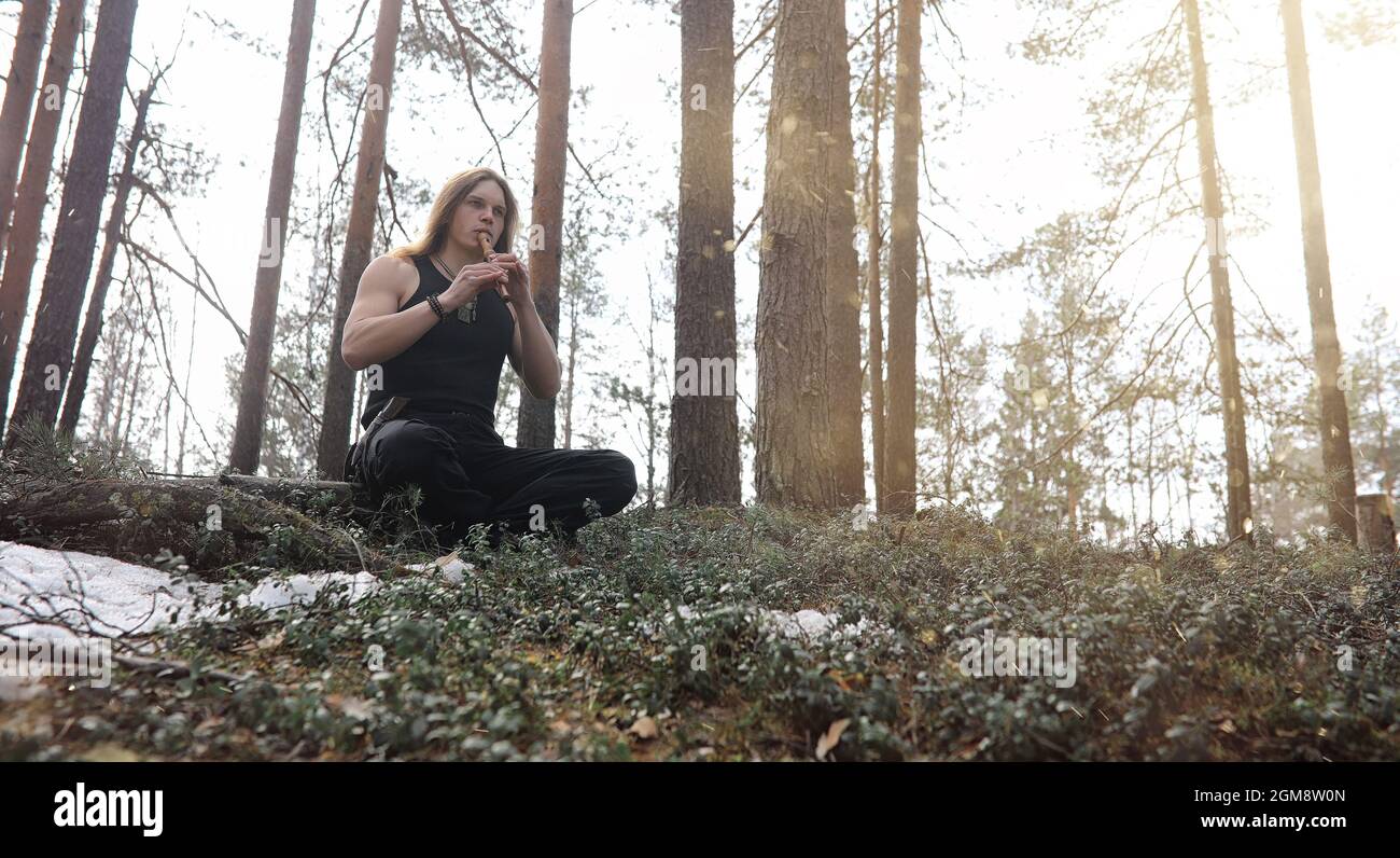 A musician with a tool in nature. Man is playing a flute in a pine ...