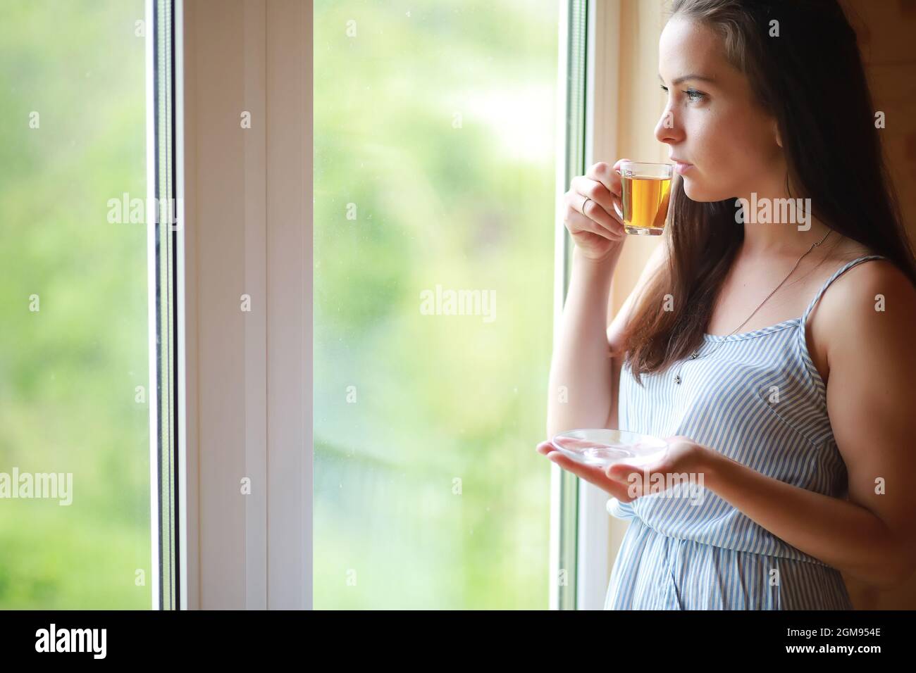 A girl at the window in the house reads a book and drinks tea Stock ...