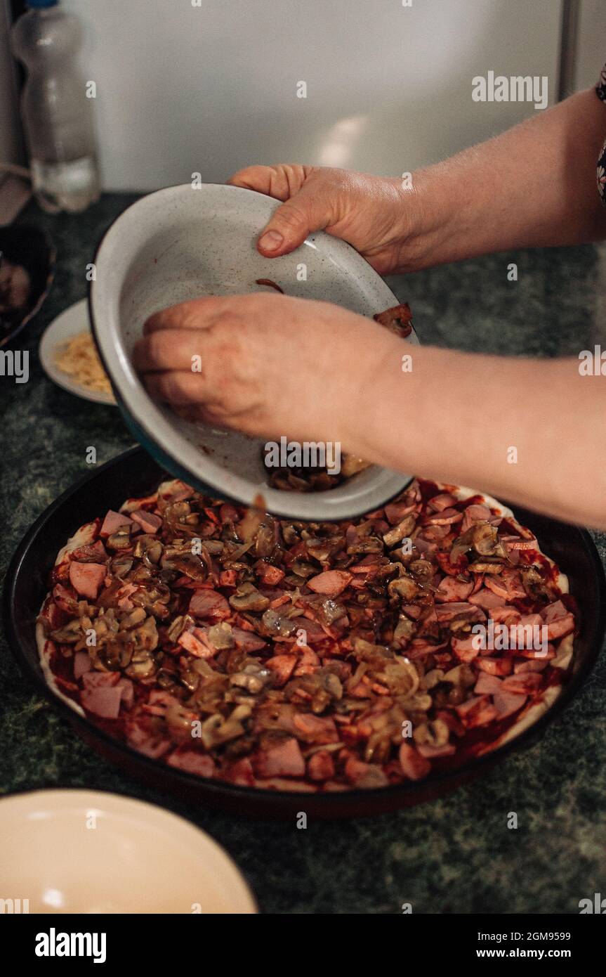 Vertical closeup of the woman preparing pizza by adding the ingredients ...