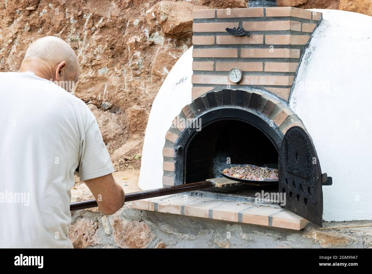 Man putting pizza in handmade white painted wood oven built outdoors ...