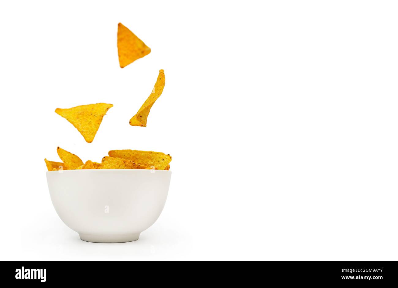 Tortilla corn chips are falling into a white ceramic bowl on a white ...