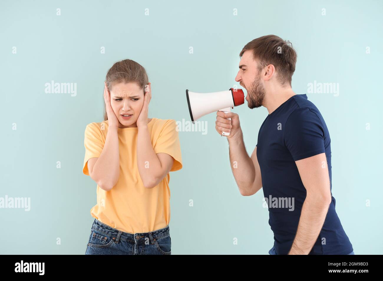 Young man shouting into megaphone at woman on color background ...