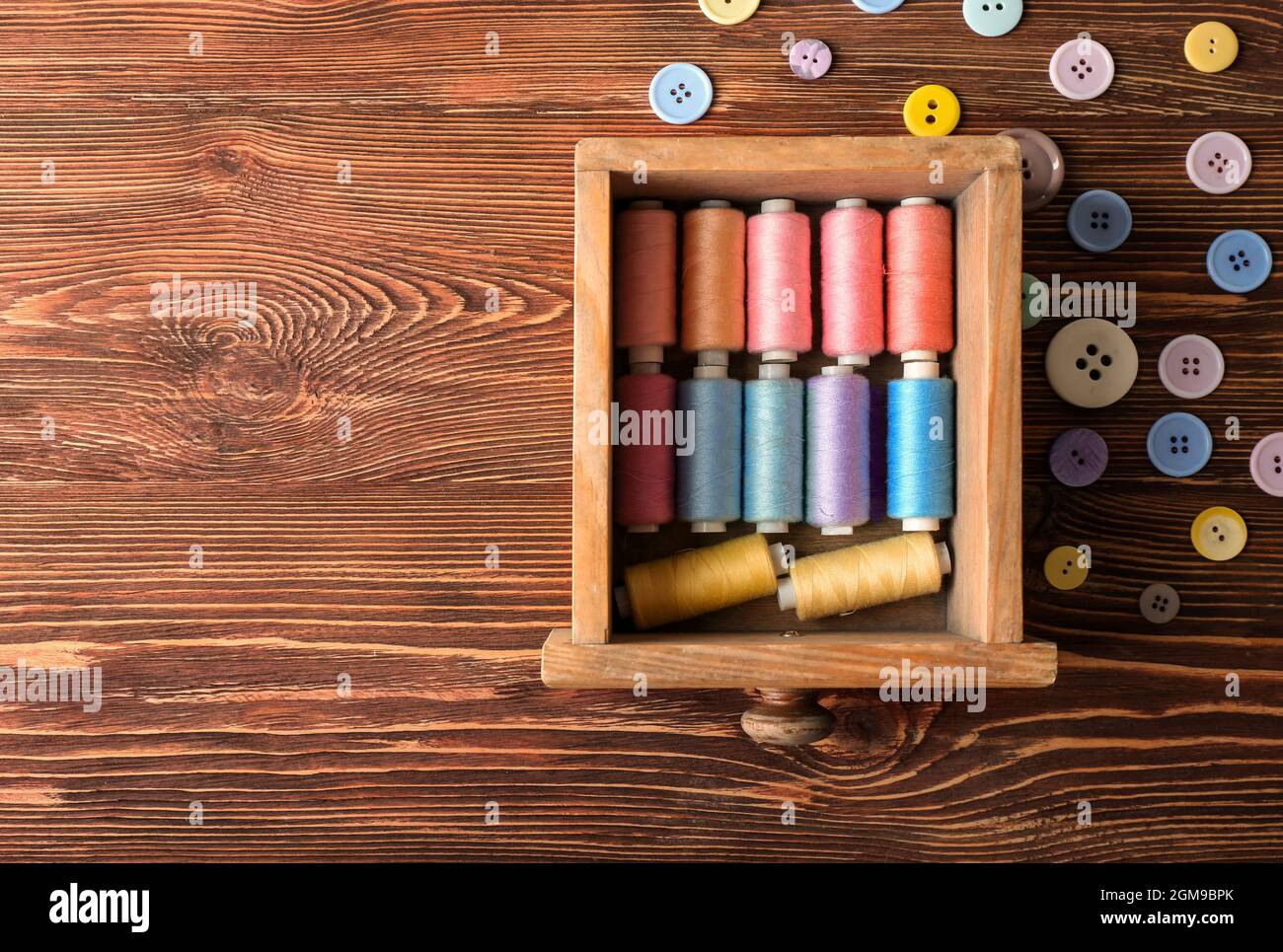Wooden drawer with color sewing threads and buttons on table, top view ...