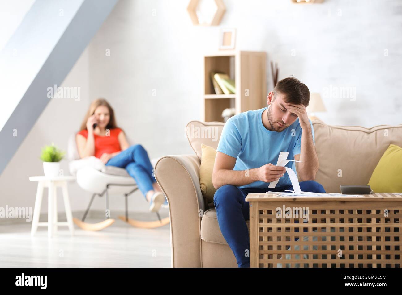 Sad man at table with bills and blurred woman on background. Money ...