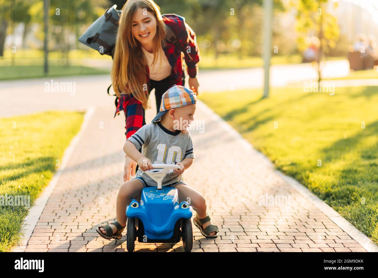 Happy cute boy ride a child's car, walking in the park with mom, mom ...