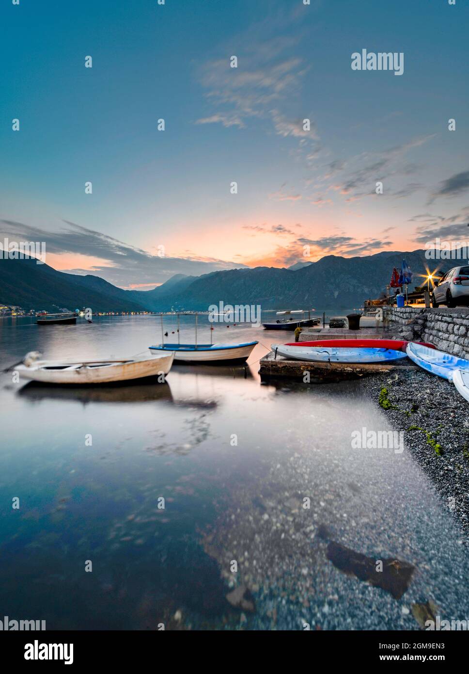 Late summer sun sets behind far mountains and boats on the Bay of Kotor ...