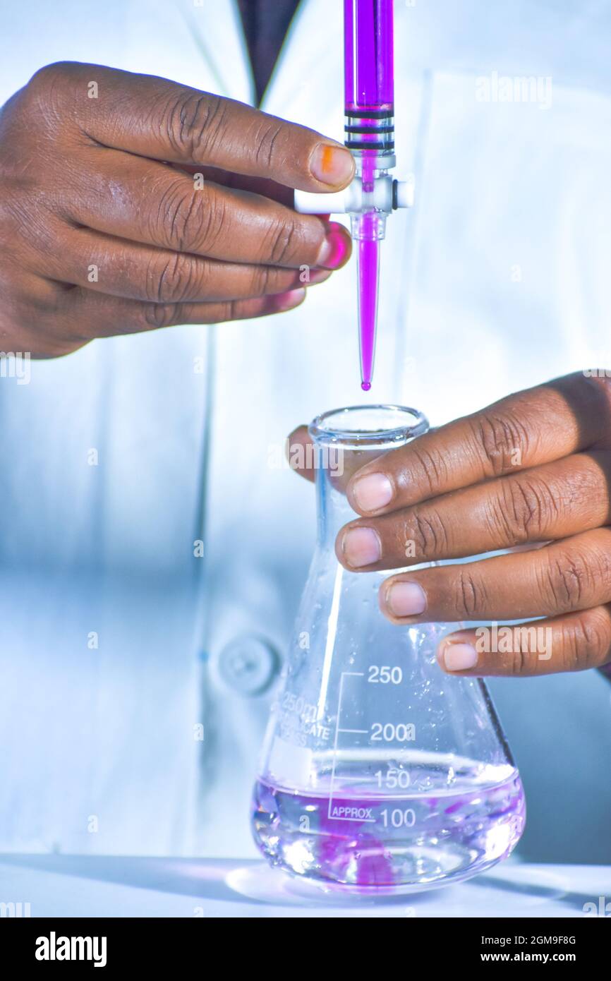 Scientist pouring color liquid into a conical flask with a dropper ...