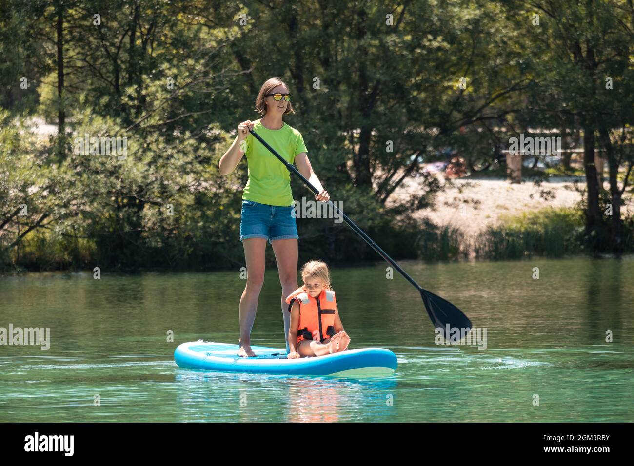 Young smiling woman paddling on a SUP - stand up paddle board, while ...