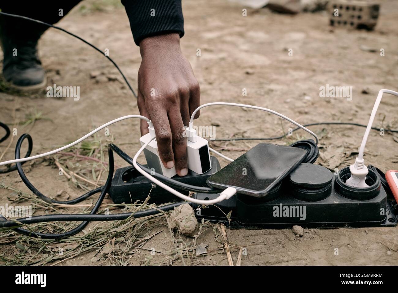 Close-up of unrecognizable black man plugging phone charger into socket ...