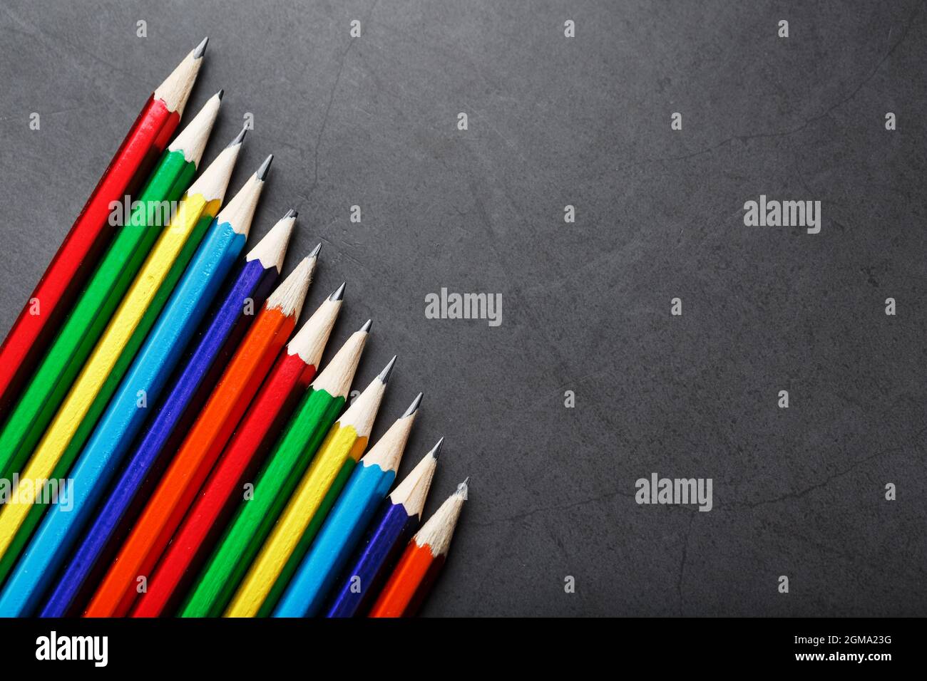 Pencils of different colors in a row on a black textured background ...