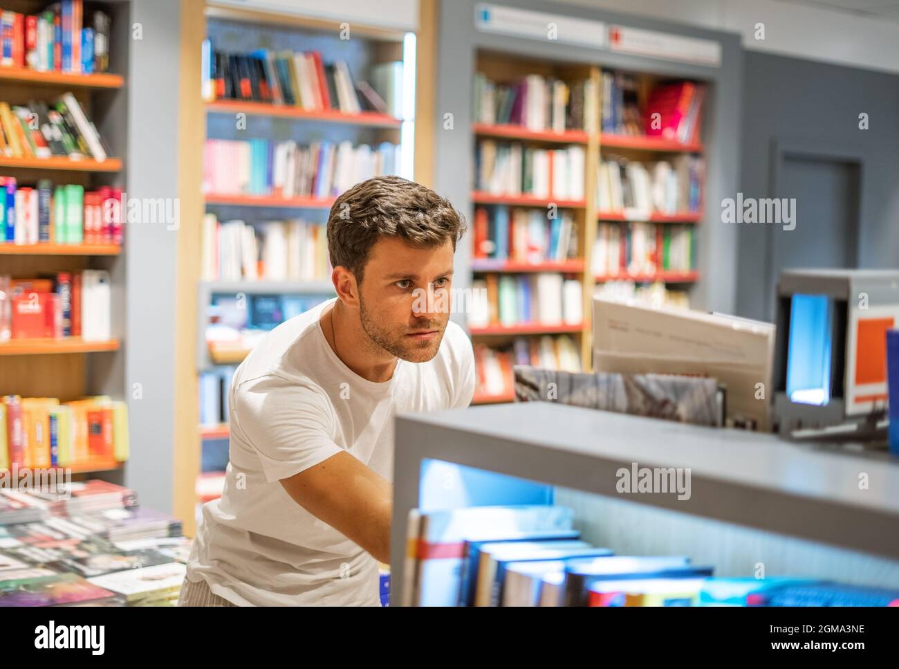 Smart young man looking through books on shelf while choosing ...