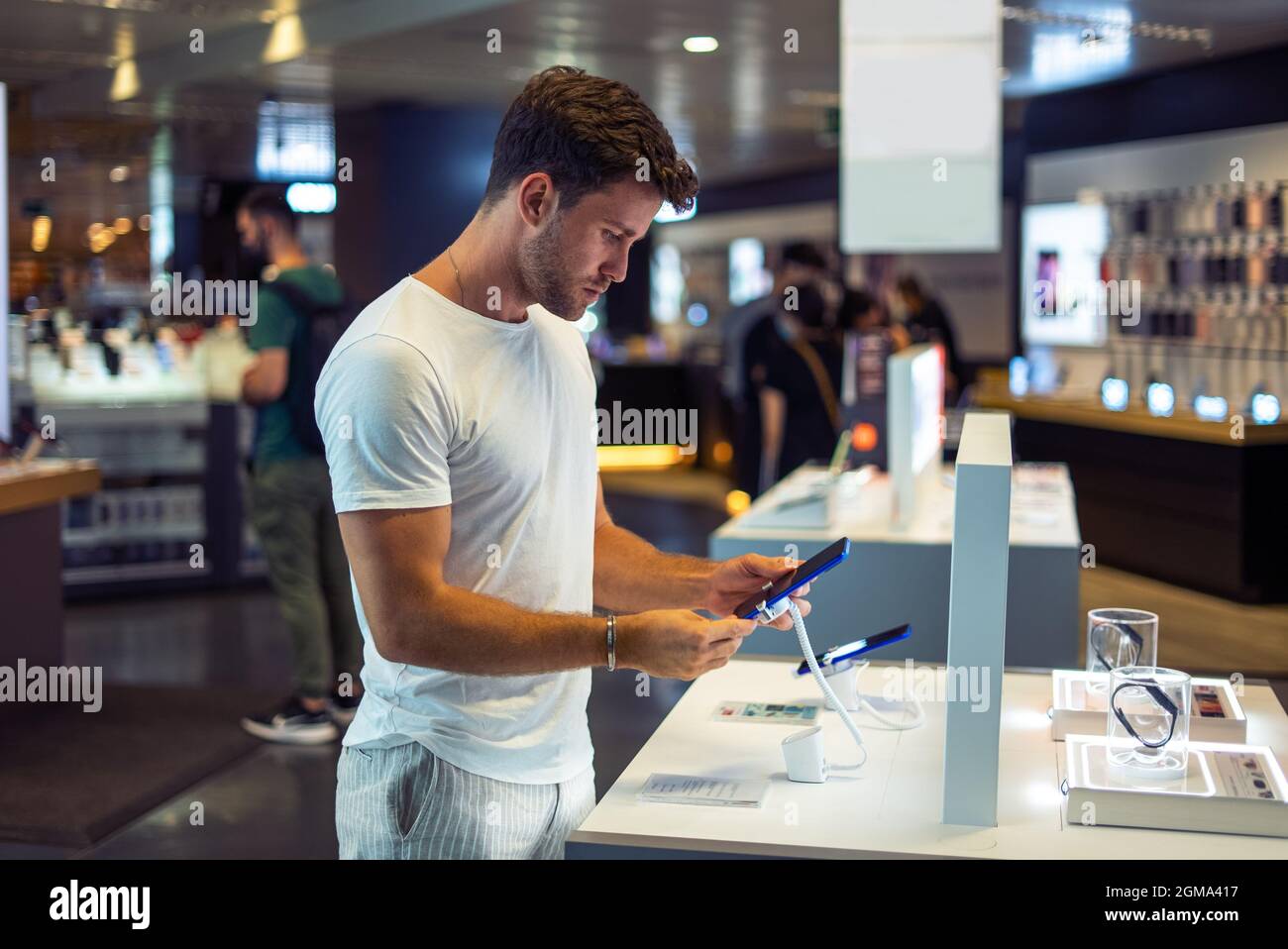 Side view of young male customer testing modern smartphone at showcase ...
