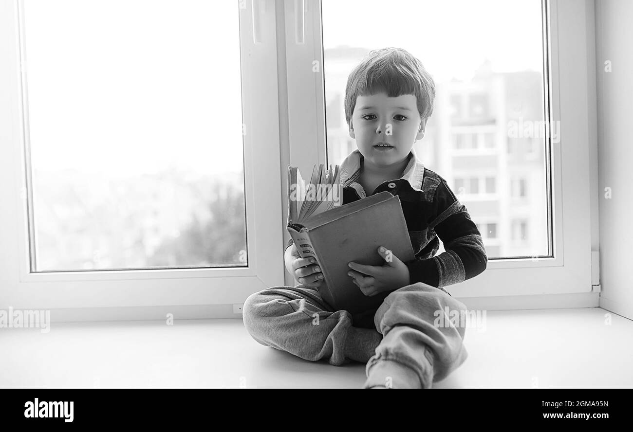 The little boy is reading a book. The child sits at the window and ...