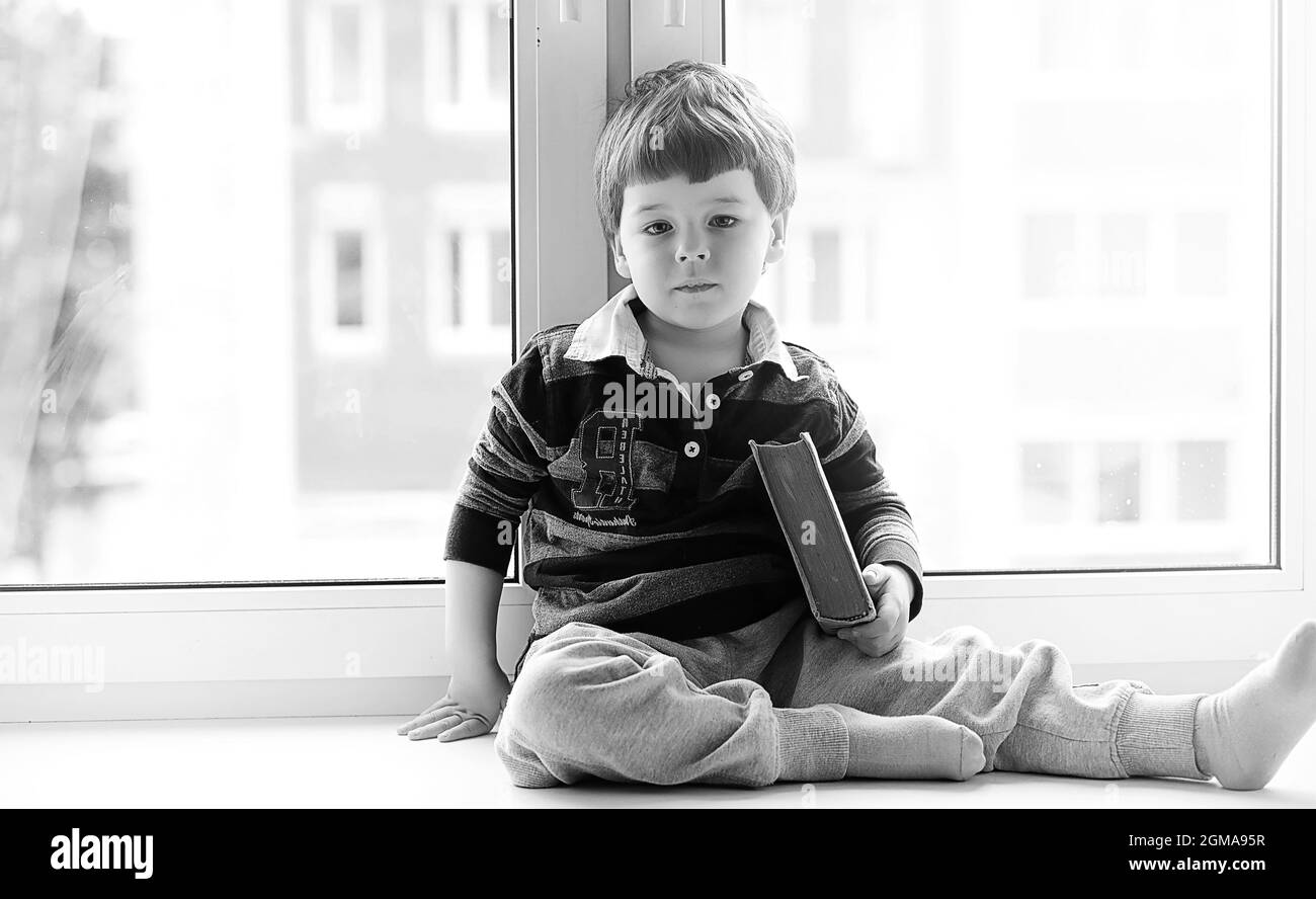 The little boy is reading a book. The child sits at the window and ...