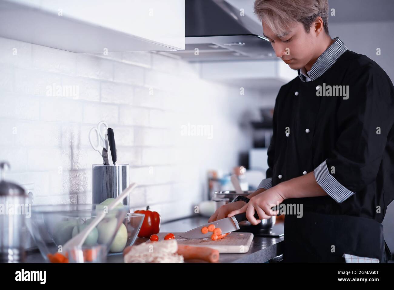 A young Asian cook in the kitchen prepares food in a cook suit Stock ...
