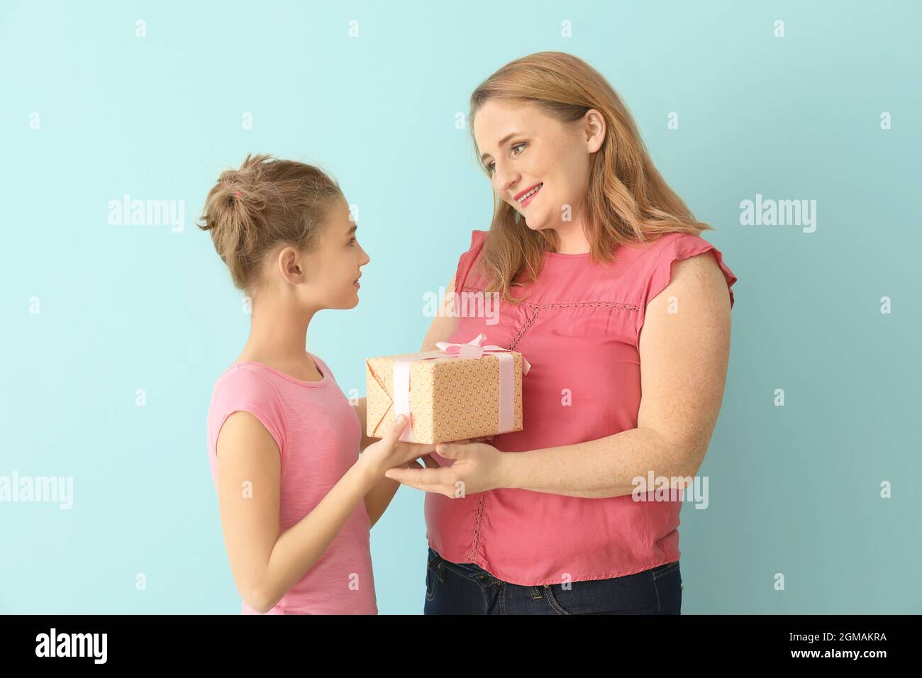 Cute little girl giving present to her mother on color background Stock ...