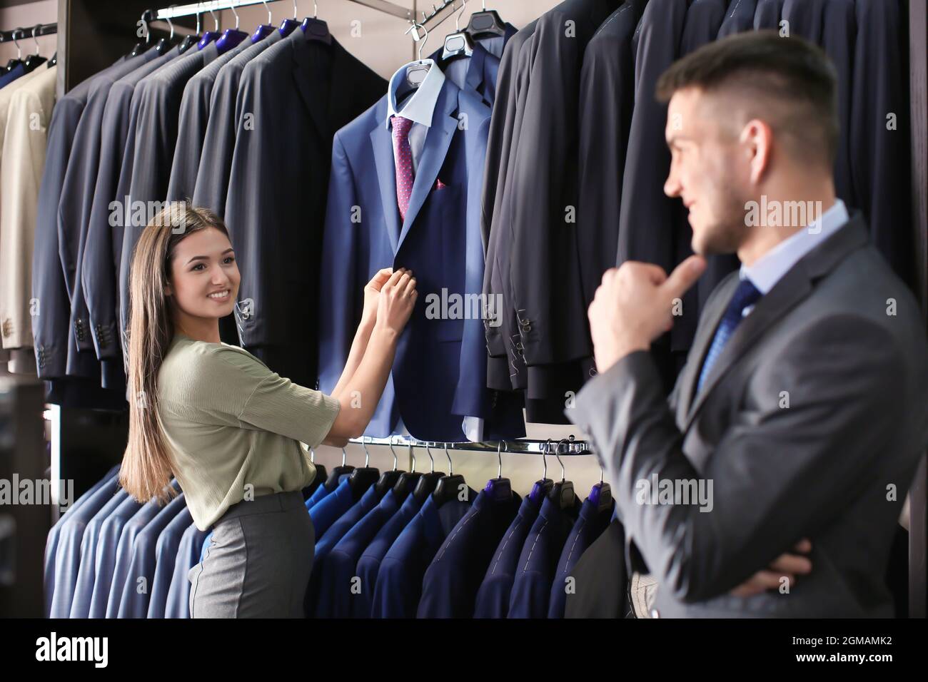 Female shop assistant helping man to choose suit in store Stock Photo ...