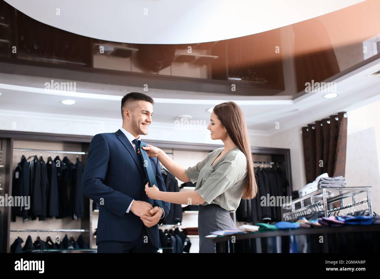 Female shop assistant helping man to choose suit in store Stock Photo ...