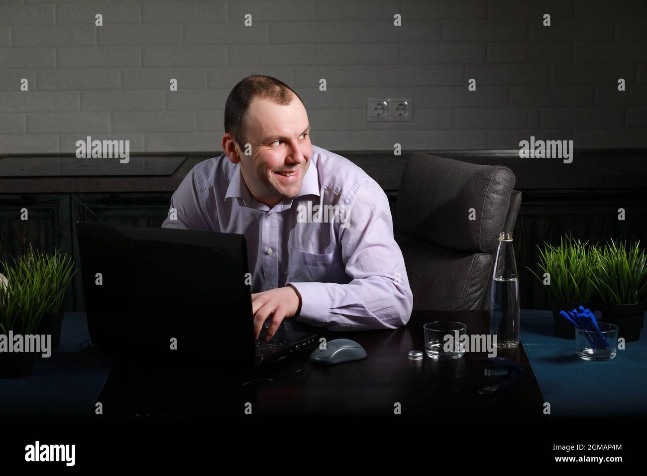 man is sitting at his desk and working on a laptop Stock Photo - Alamy