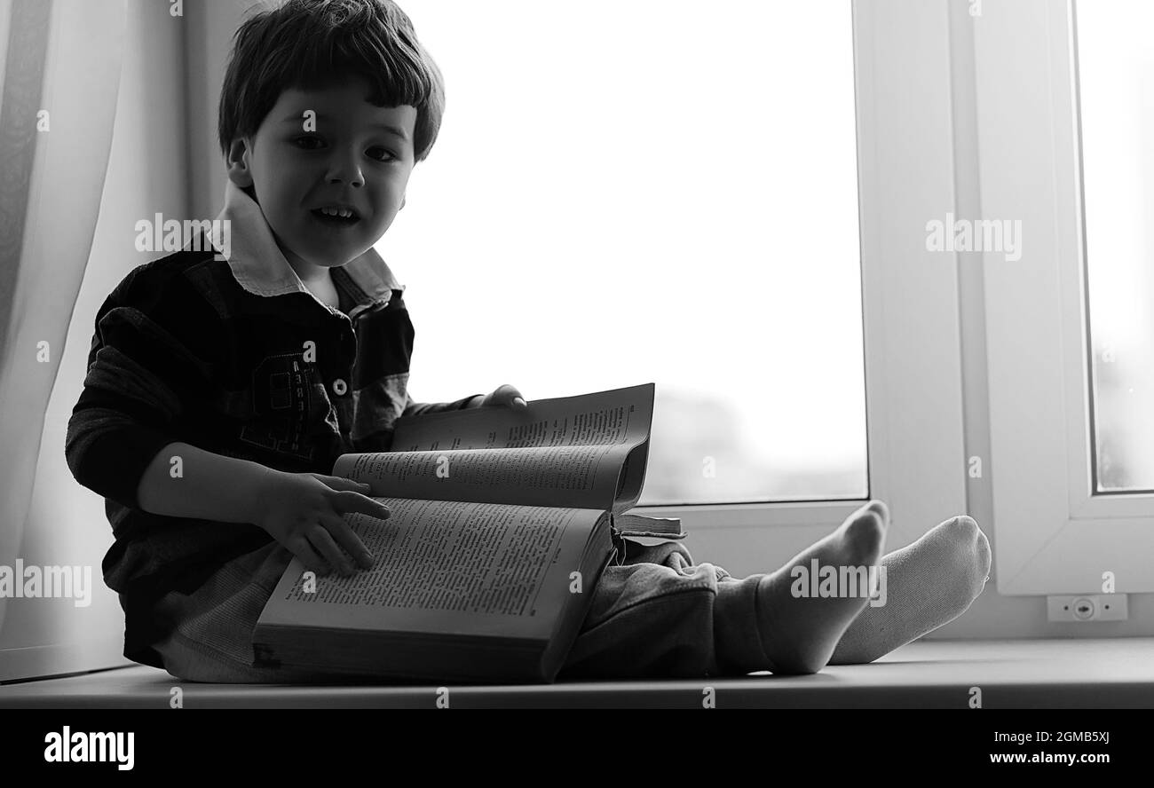 The little boy is reading a book. The child sits at the window and ...