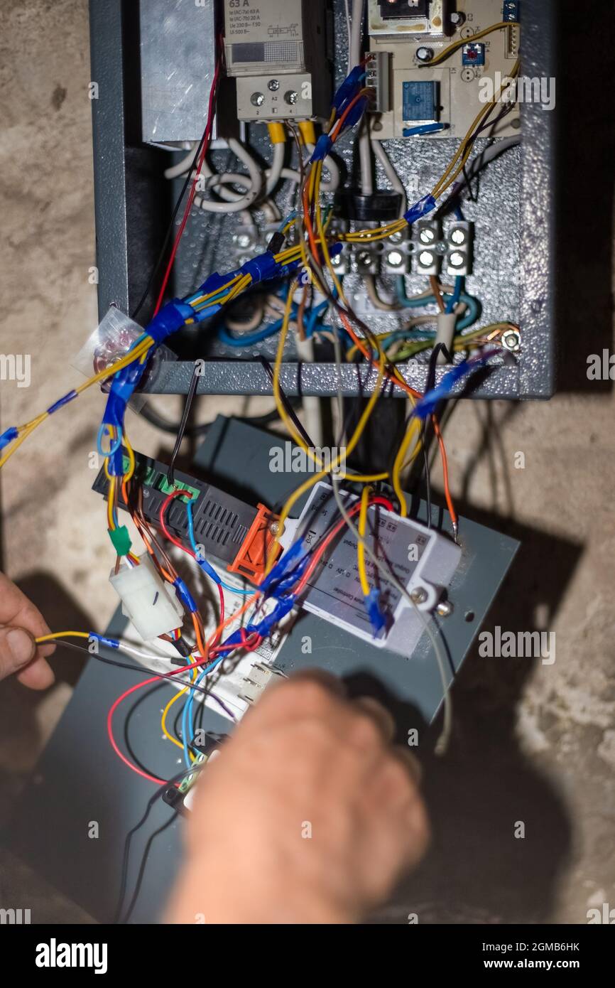 An electrician installs wires to an electric boiler to heat the house ...