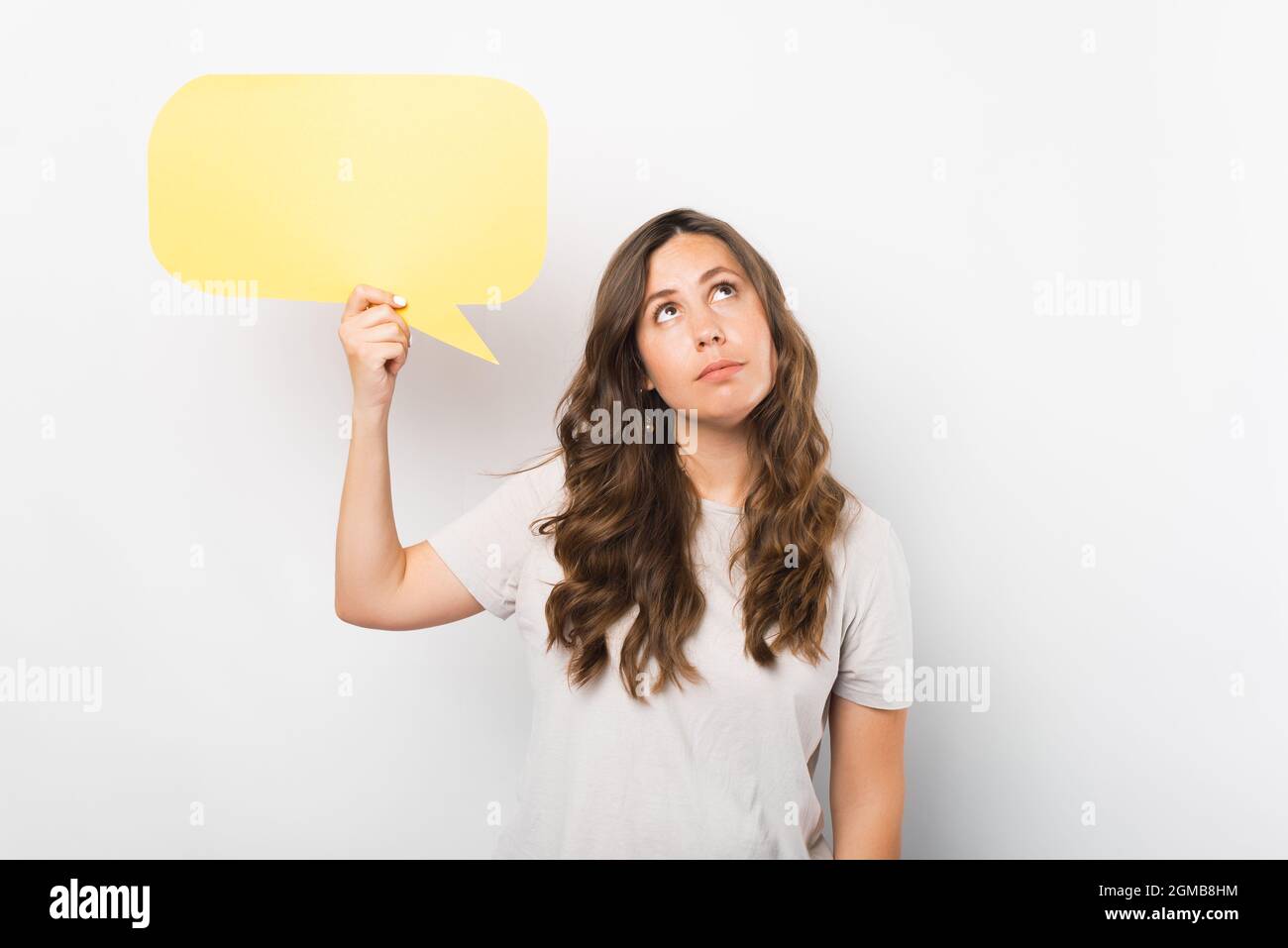 Beautiful confused woman is holding a speech bubble while looking up ...