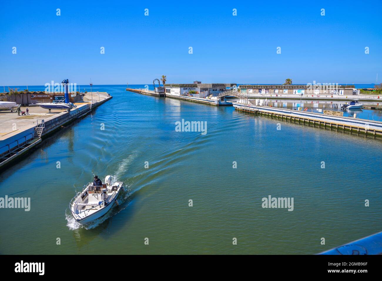 A motor boat enters a water channel on the Tuscan coast, coastal marina ...