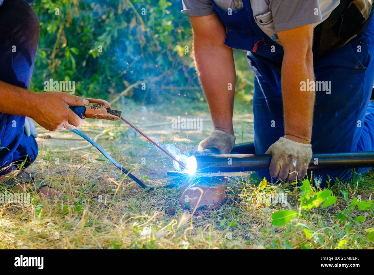 Hands of workers welding metal pipes with electric arc welding. Summer ...