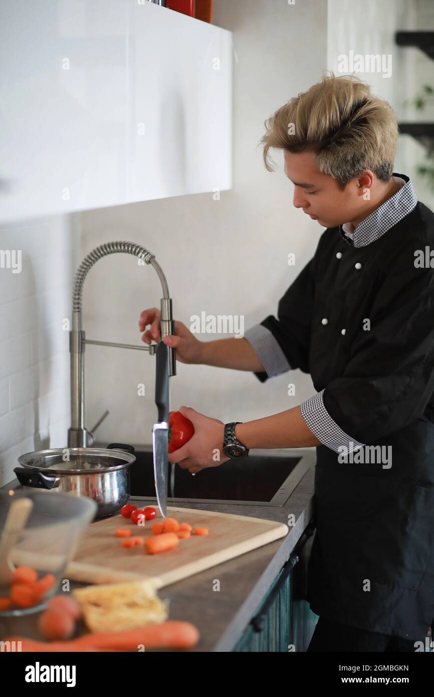 A young Asian cook in the kitchen prepares food in a cook suit Stock ...