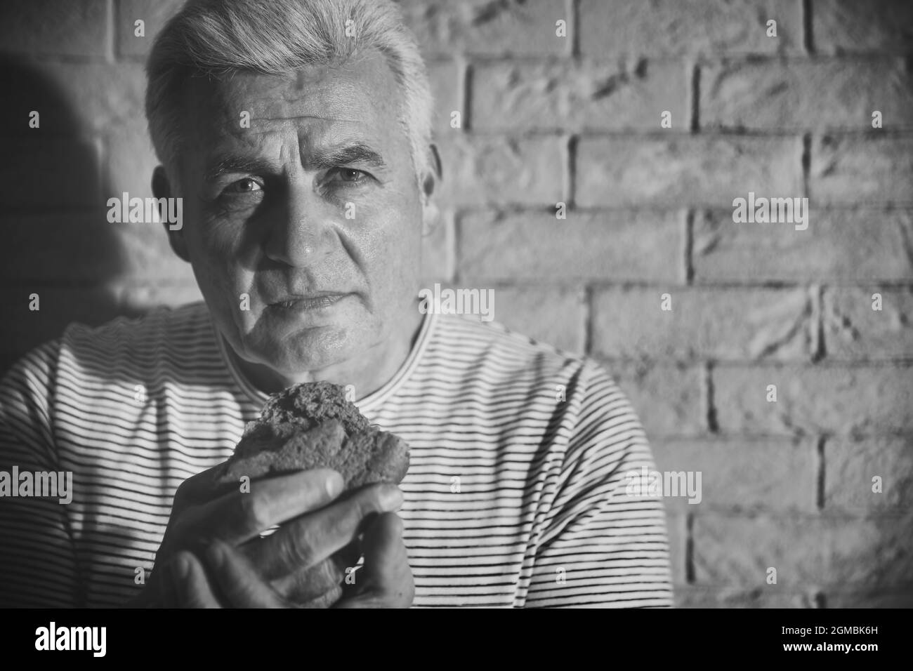 Poor man with little piece of bread on brick wall background. Black and ...
